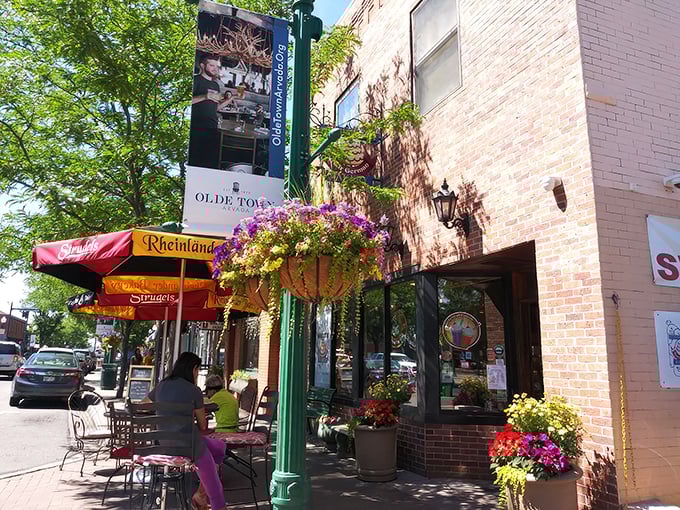 The charming exterior of Rheinlander Bakery beckons from Olde Town Arvada, where colorful awnings and flower baskets promise sweet treasures within.