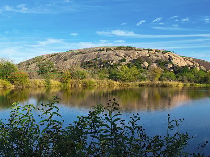 Enchanted Rock's smooth surface reflects in the calm waters below, creating a perfect mirror image of this billion-year-old natural marvel.