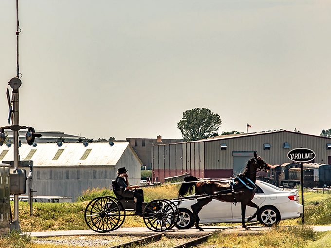 An Amish buggy waits at a railroad crossing in Strasburg, where modern cars and traditional transportation share the roads.