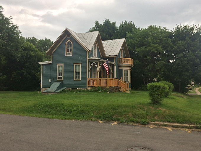 This charming blue Victorian home proudly flies the American flag, standing as a testament to craftsmanship from an era when houses had personality instead of HOA restrictions.