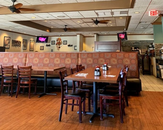 Warm wooden tones and cozy orange booths create that perfect diner atmosphere where conversations flow as freely as the coffee. The ceiling fans are just spinning stories overhead.