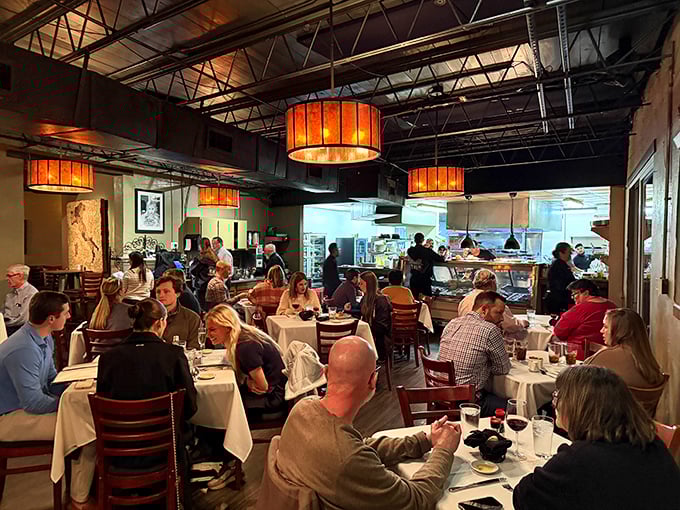 The warm glow of amber pendant lights transforms industrial ceilings into something magical, while white tablecloths promise a memorable evening ahead.
