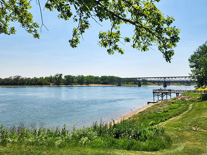 The Missouri River unfolds like nature's welcome mat, where the gentle current and distant bridge create a postcard-perfect scene that soothes the urban-weary soul.
