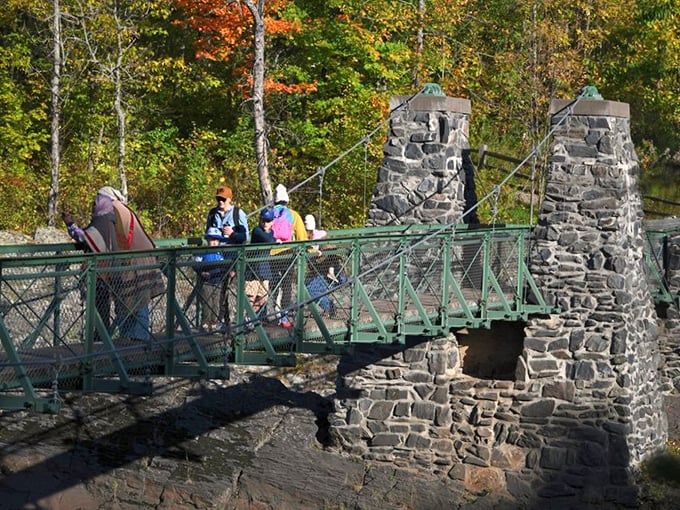 Nature's perfect frame: fall foliage creates a vibrant backdrop as visitors explore the historic stone-pillared bridge spanning the rushing St. Louis River.