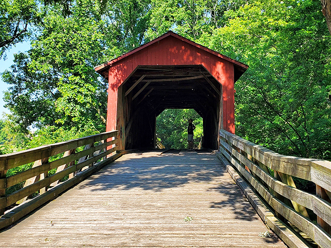 The bridge's entrance beckons with wooden planks worn smooth by generations of footsteps, each board a timeline of American rural life.