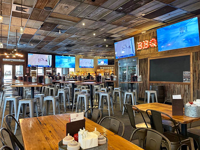 Industrial meets rustic in this spacious interior where corrugated metal ceilings, wooden accents, and strategically placed TVs create the perfect BBQ atmosphere.
