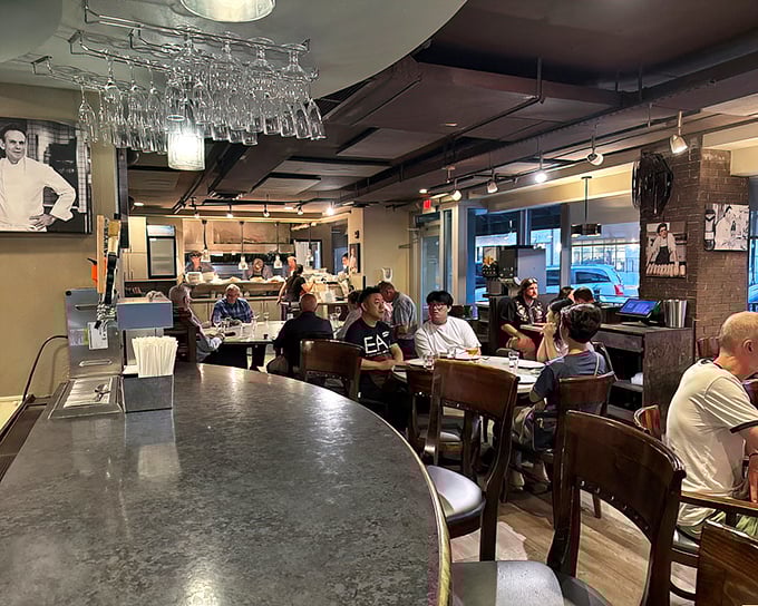 The bustling interior blends rustic charm with urban sophistication, where wine glasses dangle overhead like crystal stalactites in a cave of culinary wonders.