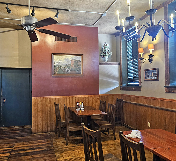 Warm wood paneling meets burgundy walls in this dining room where chandeliers cast the kind of glow that makes both food and diners look their best.