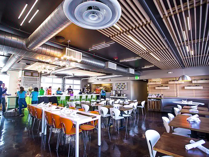 Industrial meets inviting with exposed ductwork, wooden accents, and pops of orange and green. Like a modern art gallery where the masterpieces arrive on plates.