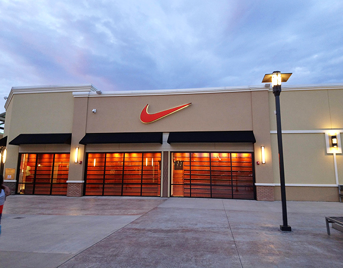 The iconic swoosh glows like a retail lighthouse at dusk, beckoning athletic enthusiasts and fashion-forward shoppers to the Nike Factory Store's treasure trove of discounted sportswear.