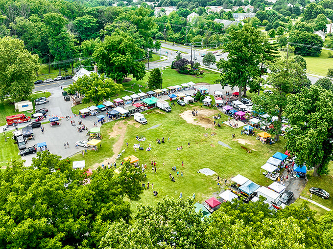 An aerial view of Olney Farmers and Artists Market, with colorful tents dotting the green landscape surrounded by trees.