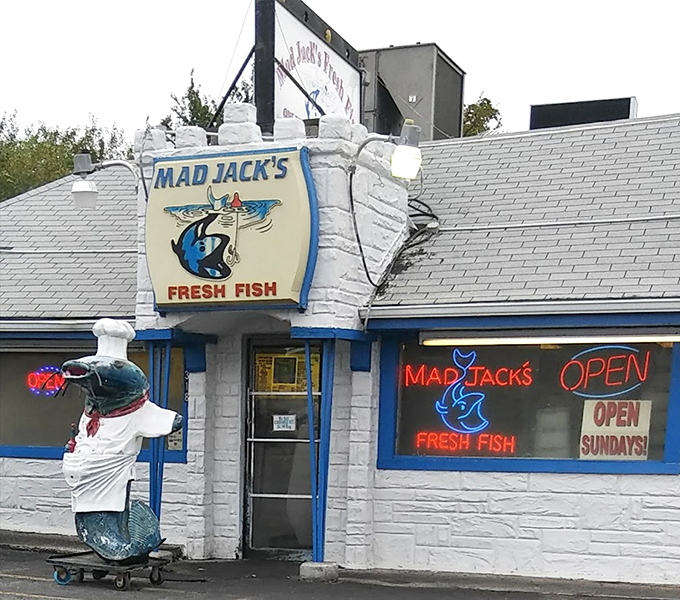 Mad Jack's distinctive white building features a playful fish mascot on a skateboard and glowing neon signs promising fresh seafood even on Sundays.