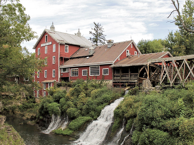 The iconic Clifton Mill perches dramatically over cascading waterfalls, its red exterior a bold statement against the lush greenery of the gorge.