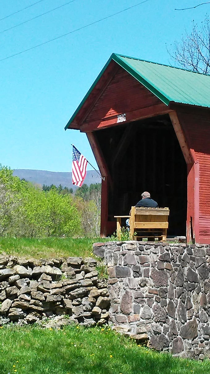 The bridge's crimson silhouette stretches across the gentle stream, its reflection dancing in the crystal-clear waters below.