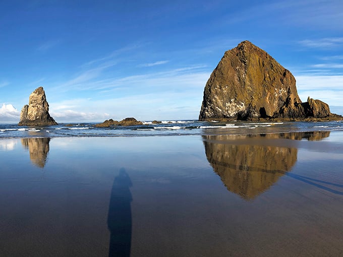 Nature's skyscraper standing sentinel in the surf. Haystack Rock's 235-foot silhouette creates perfect reflections on Cannon Beach's mirror-like sand at low tide.