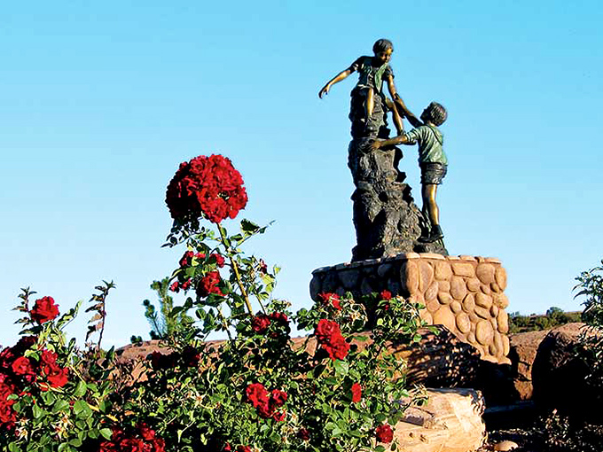 Childhood captured in bronze and surrounded by roses. This charming sculpture celebrates the simple joy of helping others up life's challenging climbs.