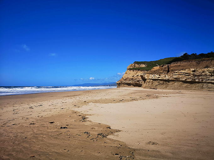 The beach stretches like nature's welcome mat, inviting you to leave footprints where towering cliffs stand sentinel.