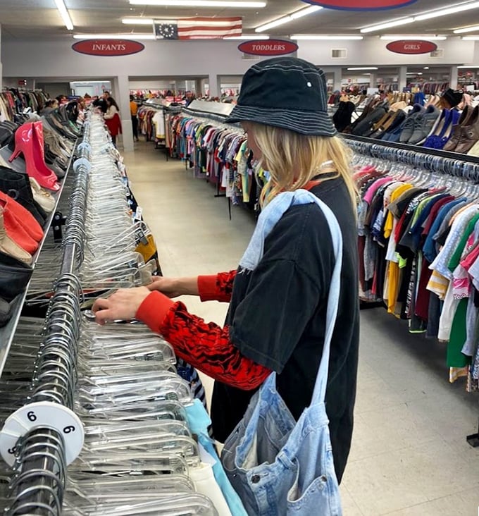 The thrill of the hunt captured in action &ndash; a shopper methodically works through racks where vintage gems hide between everyday finds.
