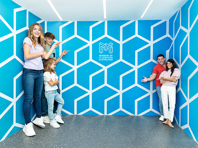 The geometric blue wall exhibit creates a mind-bending perspective illusion, making visitors appear dramatically different in size depending on where they stand.