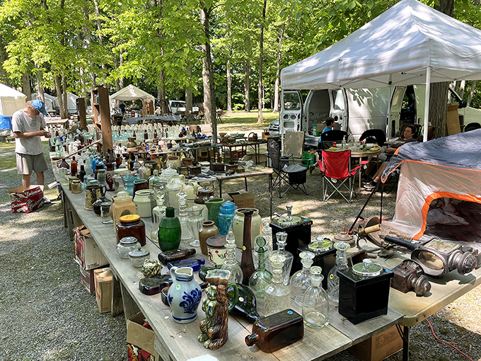 Glassware gleams in the woodland light as vendors arrange their fragile treasures, each piece telling stories of dinner parties past.