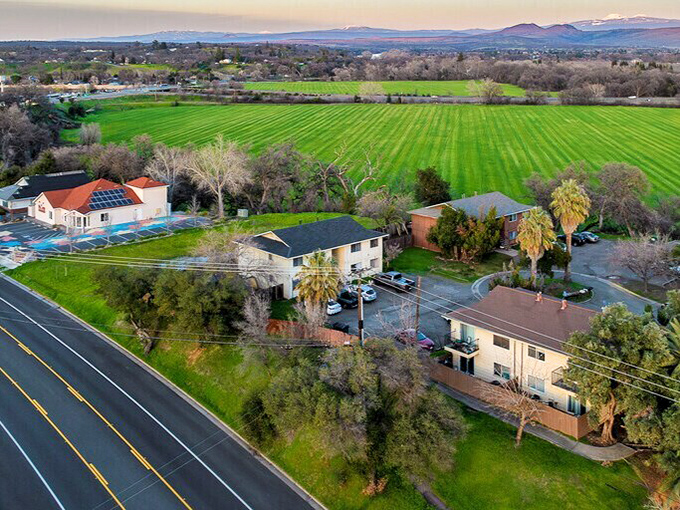 Aerial view of Red Bluff showing lush green fields, scattered homes, and distant mountains under a pastel sunset sky.