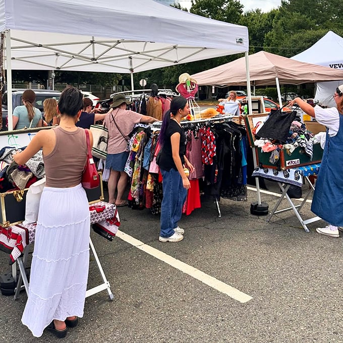 Treasure hunters crowd around colorful clothing displays at a Virginia flea market, searching for unique fashion finds under white tents.