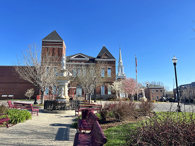 The historic courthouse square in McMinnville, Tennessee, features a striking red-brick courthouse, blooming trees, and peaceful benches under a clear blue sky.