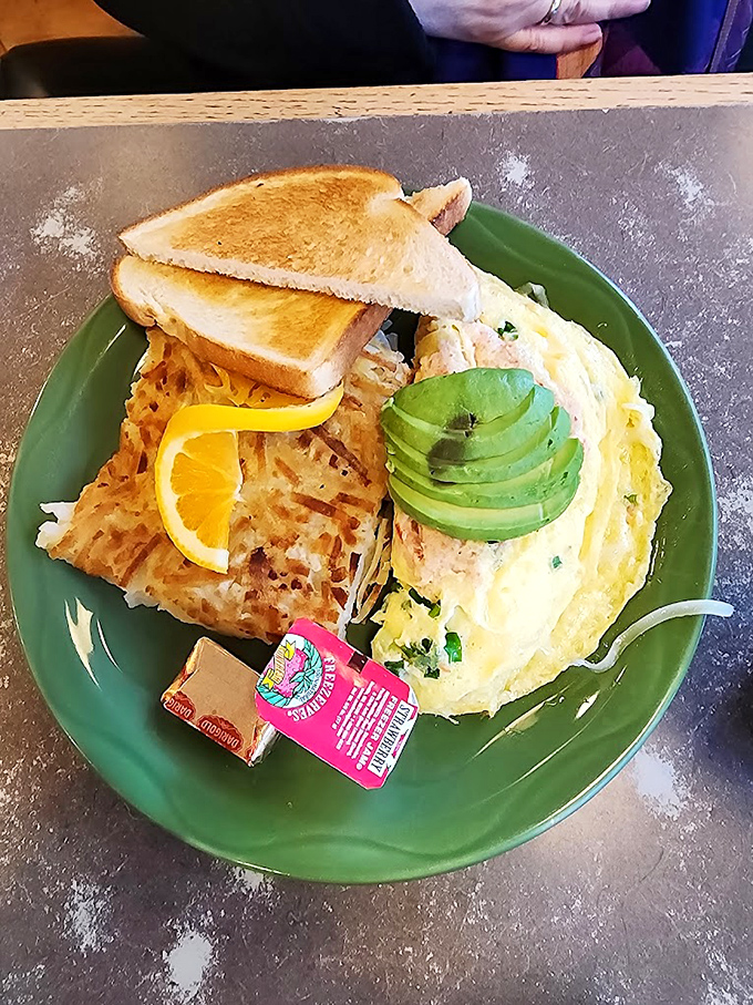 Breakfast artistry at its finest: golden hash browns, perfectly folded omelet, fresh avocado, and toast that actually deserves to be called "toast."
