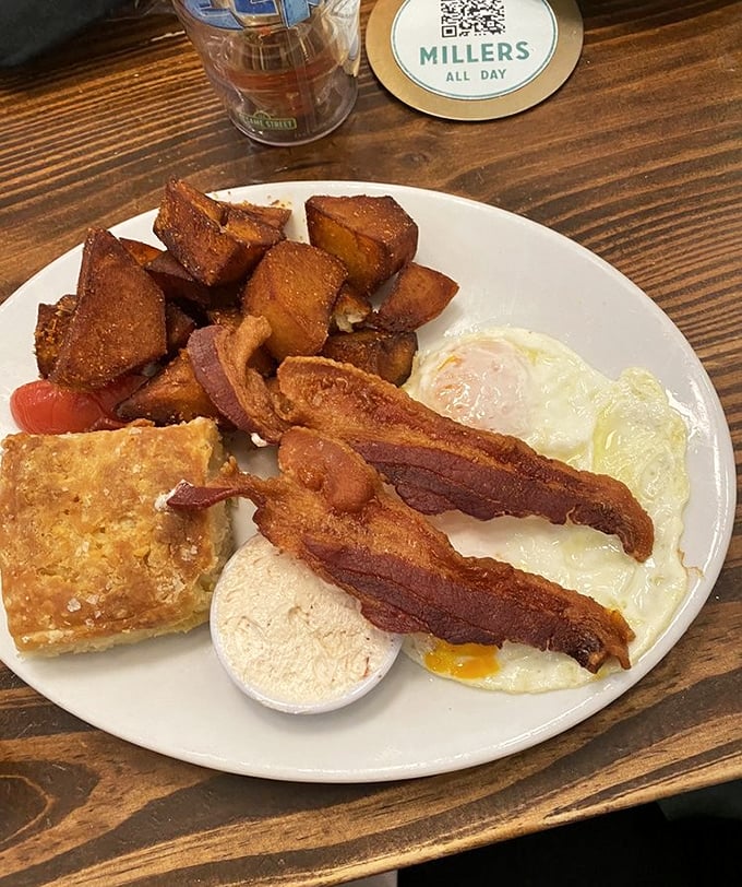 Breakfast perfection on a plate: crispy home fries, thick-cut bacon, sunny eggs, and a golden biscuit corner. This is how mornings were meant to begin.