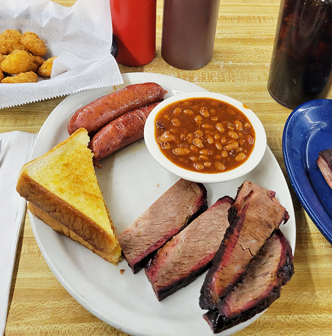 Behold the holy trinity of BBQ perfection: brisket with that telltale smoke ring, sausage links, and baked beans swimming with bits of meat.