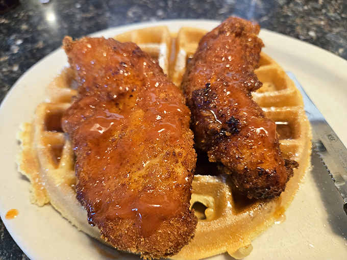 Golden chicken tenders resting on a waffle like they've found their forever home, drizzled with syrup perfection throughout.