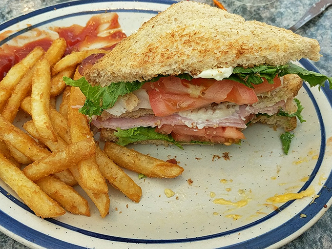 The club sandwich arrives like a skyscraper of flavor, layered with fresh ingredients and flanked by golden fries that demand immediate attention.