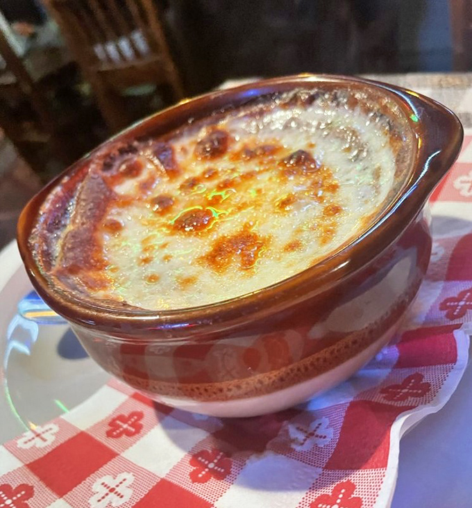The legendary French onion soup arrives like a treasure chest—crack through that golden cheese canopy to discover the sweet, savory riches hiding beneath.