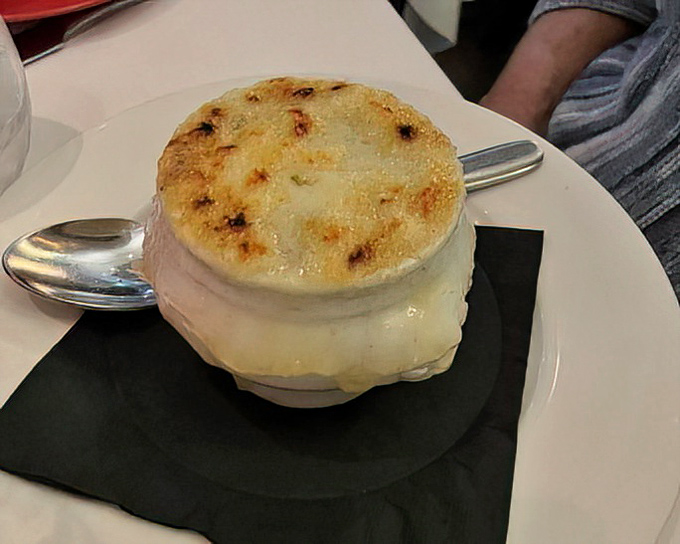 The legendary French onion soup arrives like a work of art &ndash; that golden, bubbling cheese canopy hiding a rich, deeply flavored broth beneath.