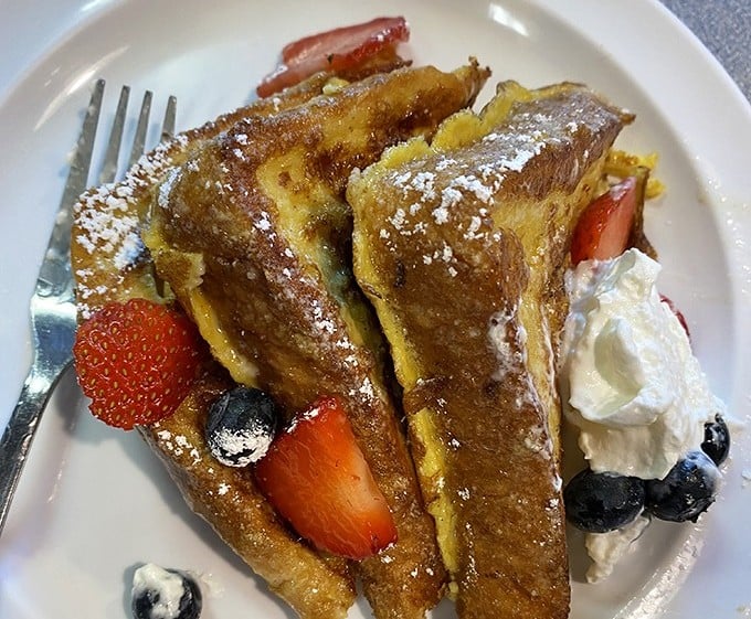 French toast nirvana achieved: golden-brown perfection adorned with fresh berries and a cloud of whipped cream that melts all willpower.