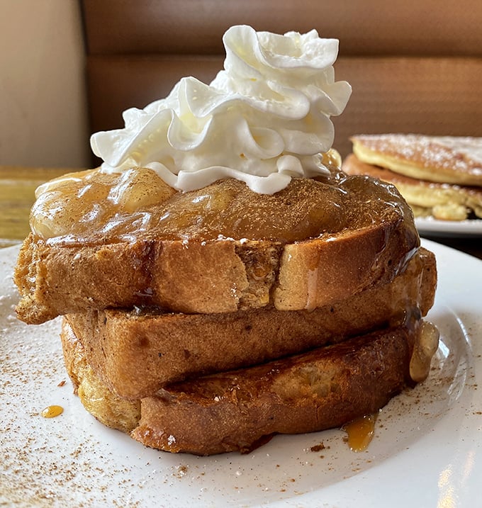 French toast architecture at its finest&mdash;golden-brown layers stacked with military precision, crowned with a cloud of whipped cream. Breakfast royalty deserving of your devotion.