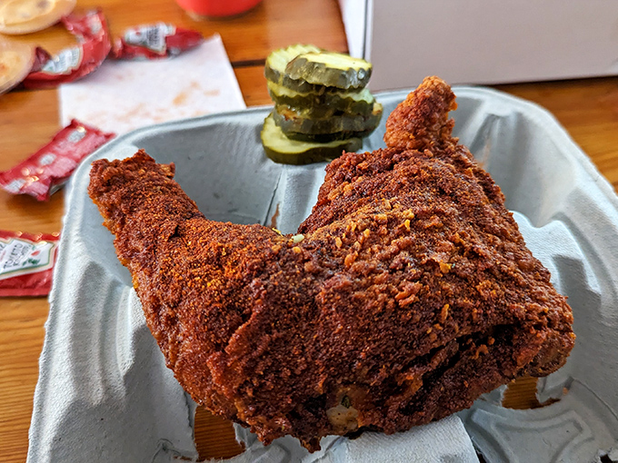 Behold the masterpiece: a quarter dark meat chicken, wearing its fiery red spice coat like a badge of honor, with cooling pickles standing guard.