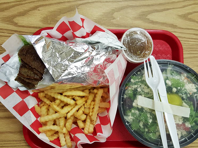 A proper meal: golden fries, Greek salad, and what appears to be a steak sandwich wrapped in foil – the holy trinity of lunch perfection.