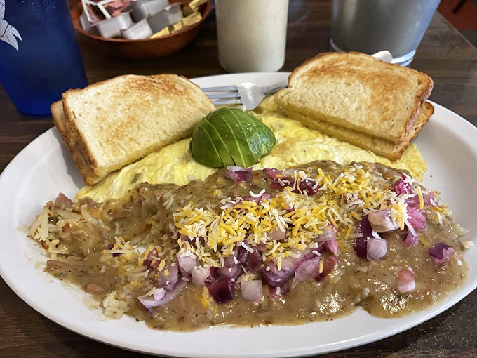 Behold breakfast alchemy: a perfect omelet draped with green chile sauce, crowned with cheese and red onions, with perfectly golden toast standing guard.