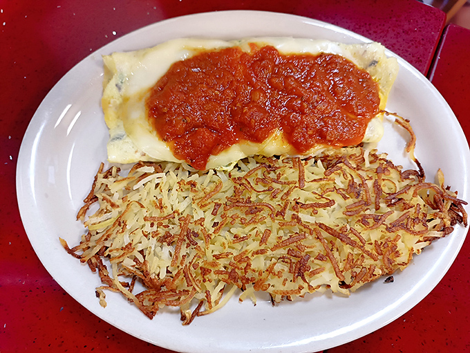 The Italian omelet arrives like a golden sunrise, topped with marinara and paired with hash browns that achieved the crispy-fluffy holy grail.