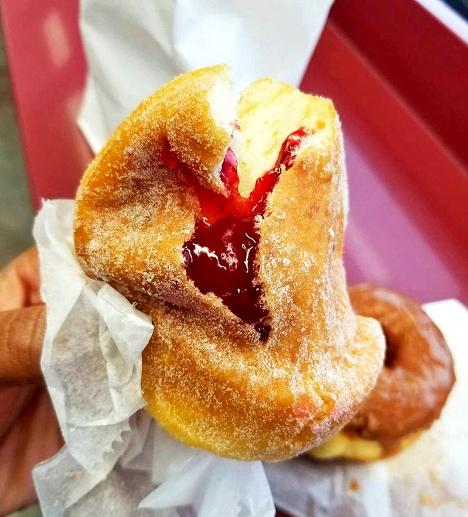 The jelly donut reveals its ruby treasure like a geologist cracking open a geode. Sweet science at its most delicious.