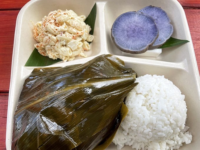 Behold the star attraction: lau lau in its leafy glory, accompanied by creamy macaroni salad and purple sweet potato that looks like edible art.