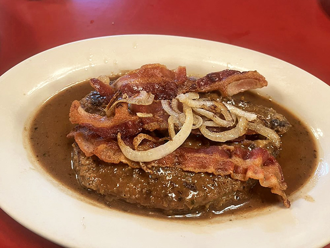 Behold the burger in all its glory, swimming in savory gravy with a crown of crispy bacon and onions—comfort food that hugs your soul.