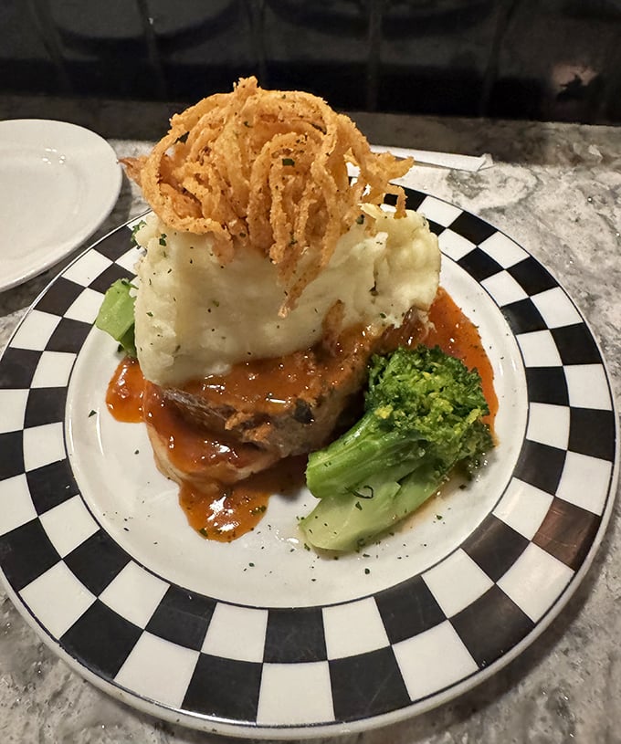 The legendary meatloaf arrives like royalty – crowned with crispy onion straws and surrounded by its loyal subjects: mashed potatoes and gravy.