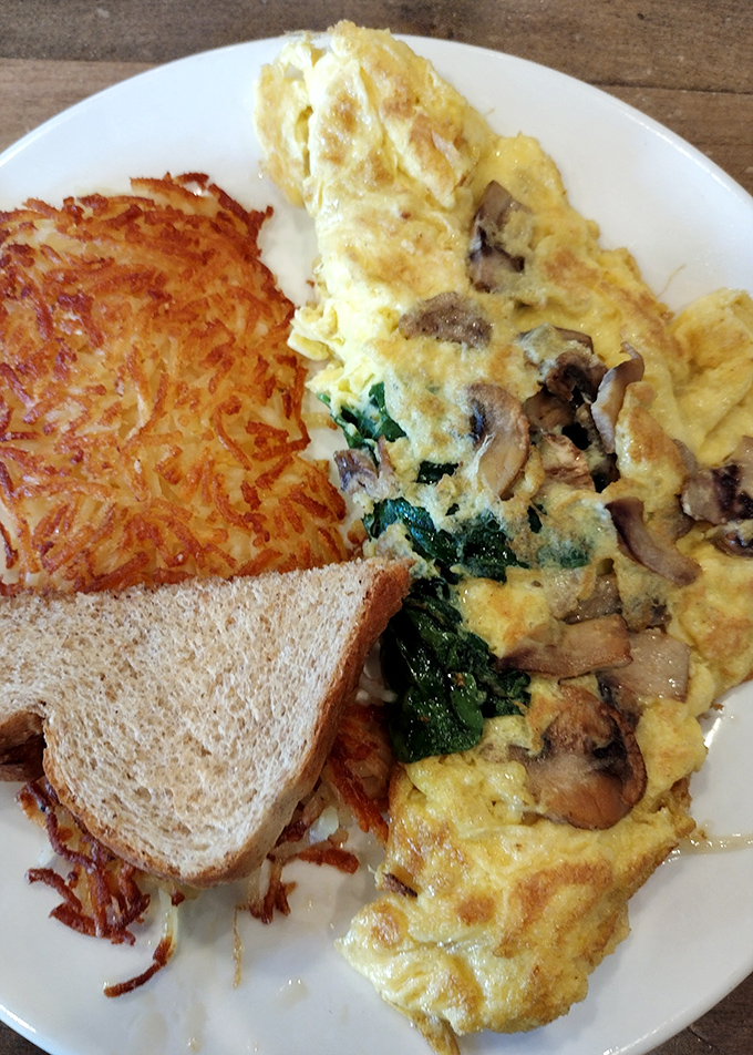 Behold the holy trinity of breakfast perfection: a mushroom-spinach omelet that's fluffier than a cloud, crispy hash browns, and toast standing by for cleanup duty.