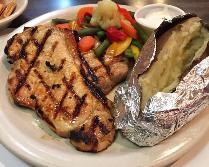 Not just any pork chop &ndash; this golden-grilled beauty shares the plate with a rainbow of vegetables and a baked potato waiting for its moment.