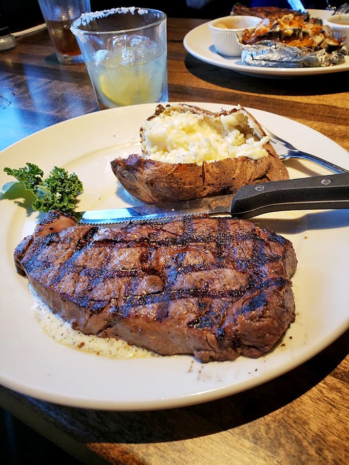 Behold the ribeye in its natural habitat &ndash; perfectly charred outside, tender inside, with a loaded baked potato standing by for backup.