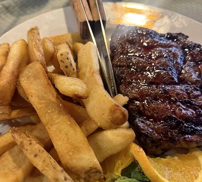 Behold the ribeye in all its glory, perfectly seared with those beautiful grill marks, accompanied by golden fries that look hand-cut and properly crisp.