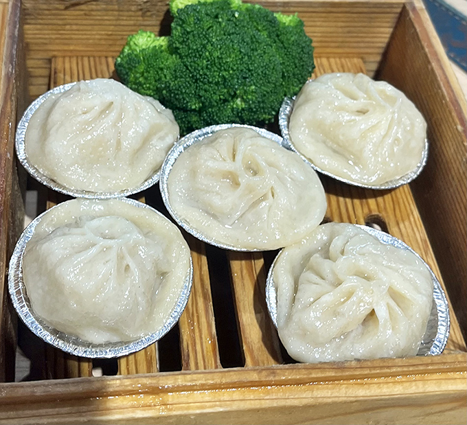 These Shanghai dumplings aren't just food; they're little pouches of joy, delicately pleated and steamed to perfection in their aluminum thrones.
