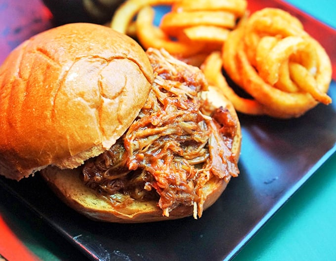 This pulled pork sandwich isn't just a meal—it's an event. The meat practically collapses under its own tenderness, while those curly fries stand at attention.